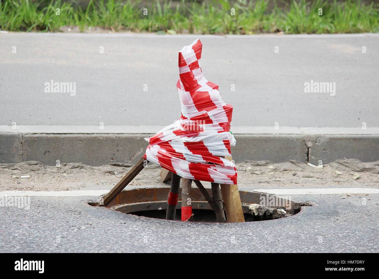 Dangerous open hatch without cover and a warning fence on the road ...