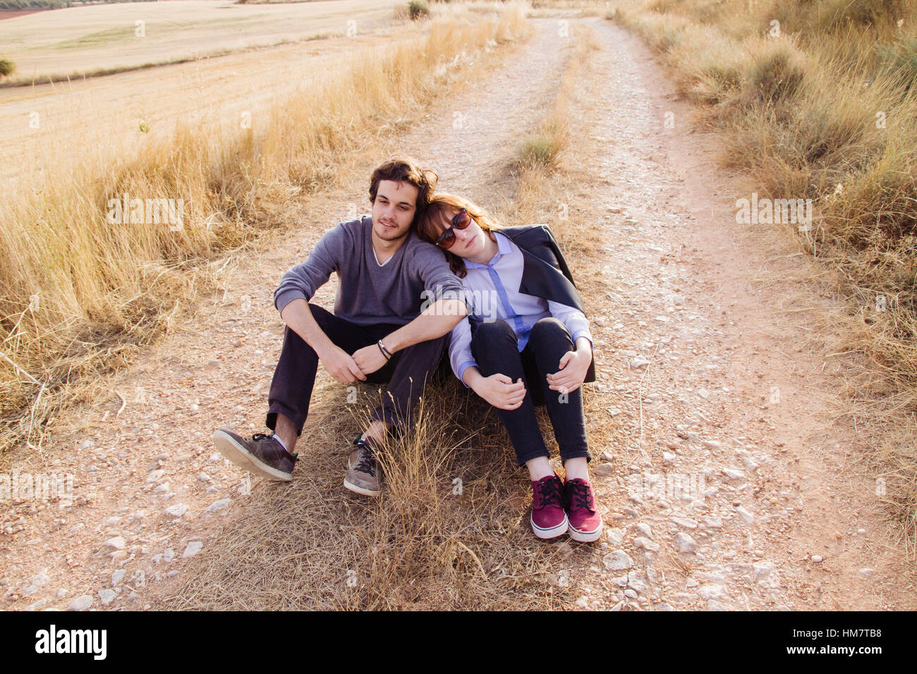 Young hipster couple sitting in a rural path Stock Photo - Alamy