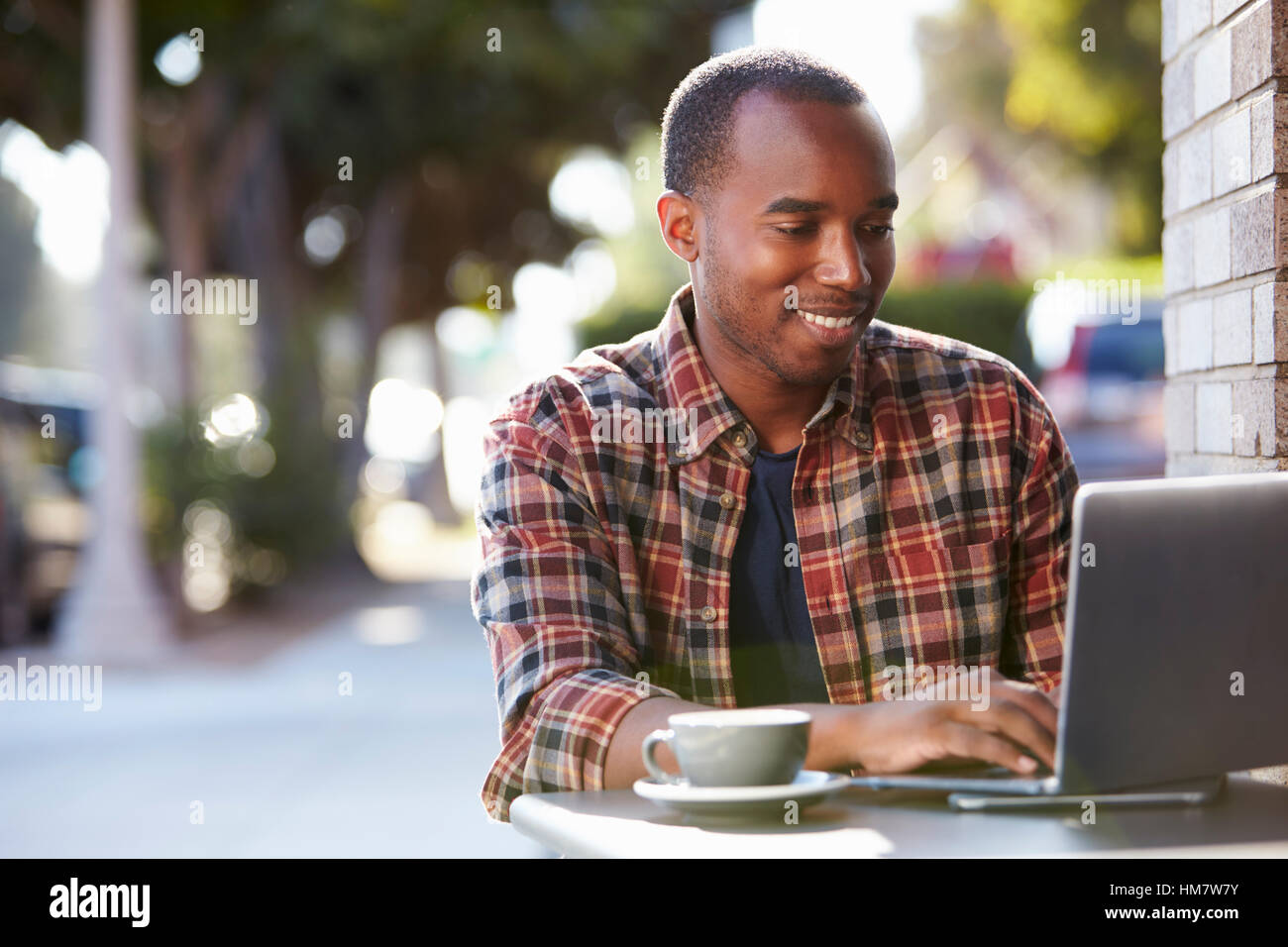 Young black man using a laptop computer outside a cafe Stock Photo - Alamy