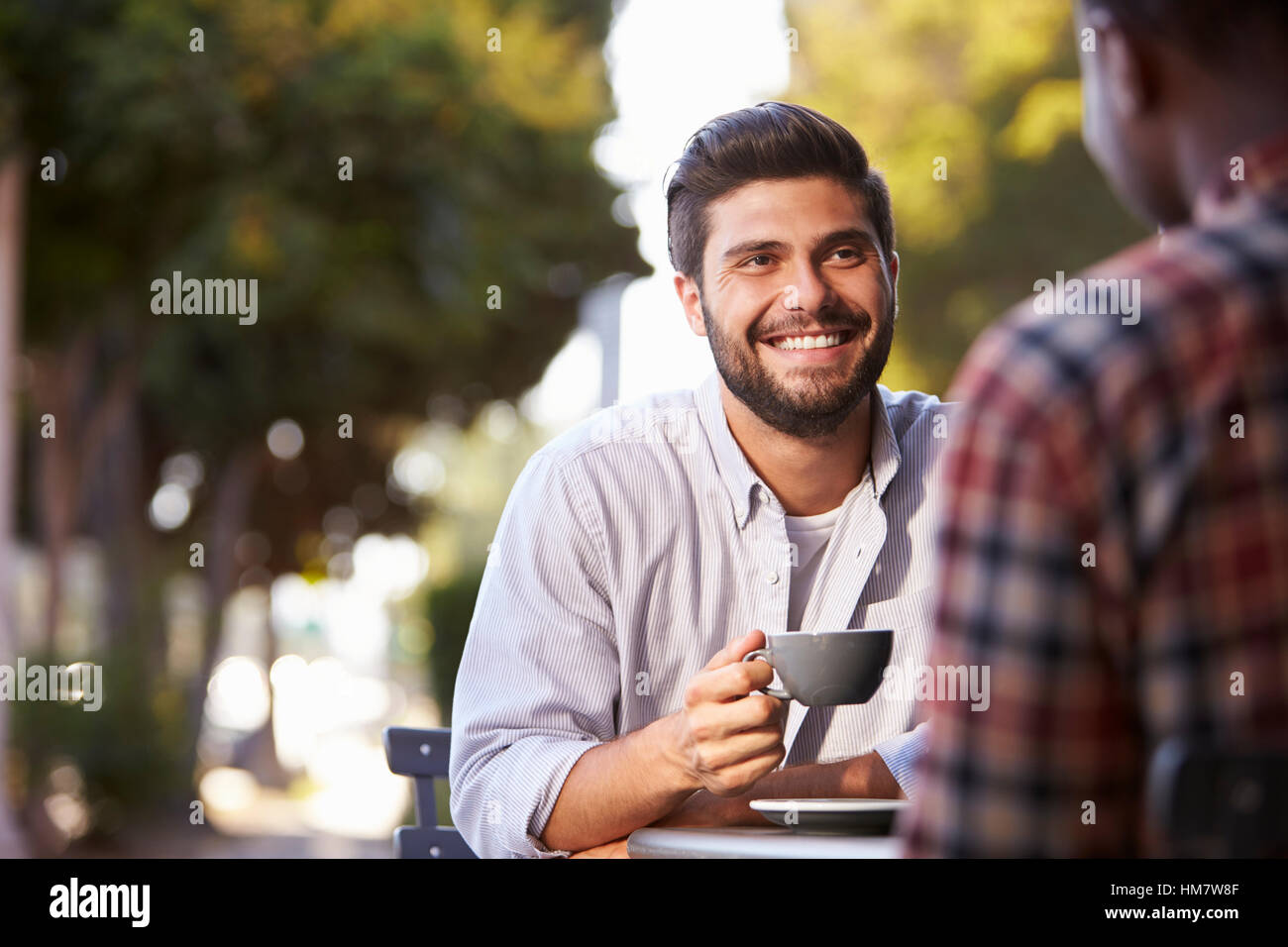 Two adult male friends sit talking over coffee outside cafe Stock Photo ...
