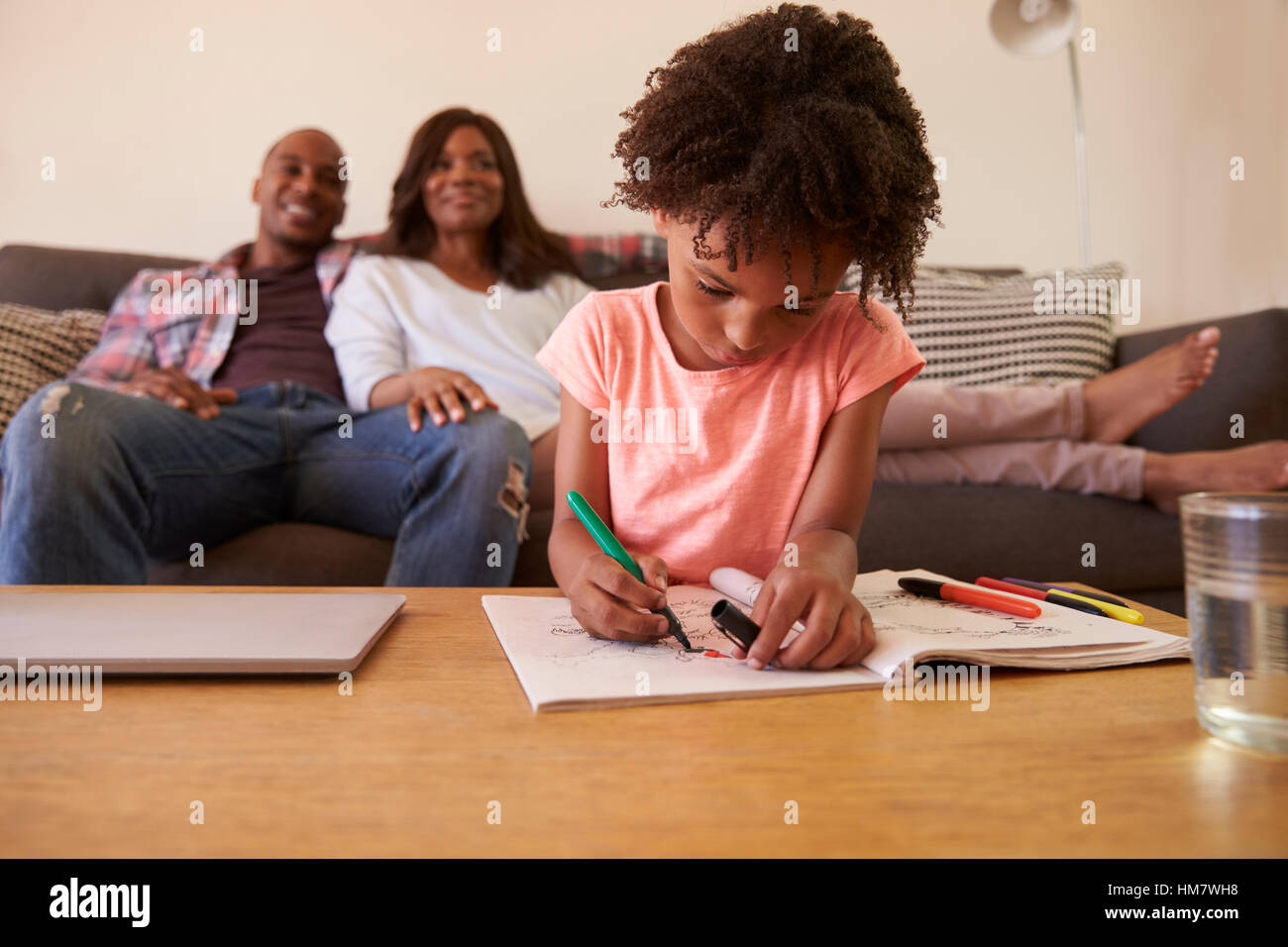 Parents Watch TV As Daughter Colors In Picture Book Stock Photo - Alamy