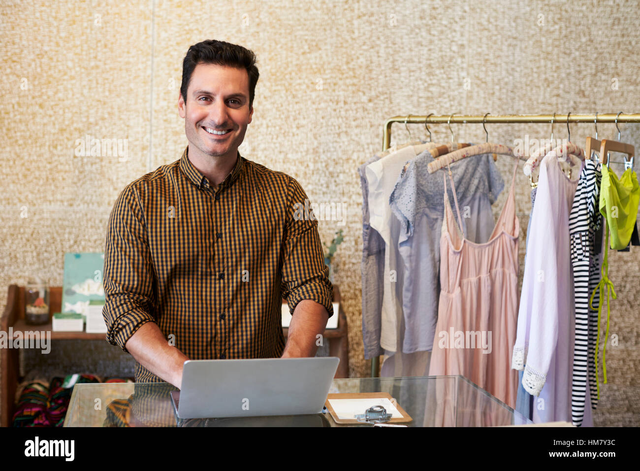 Young man working in clothes shop using laptop at counter Stock Photo ...