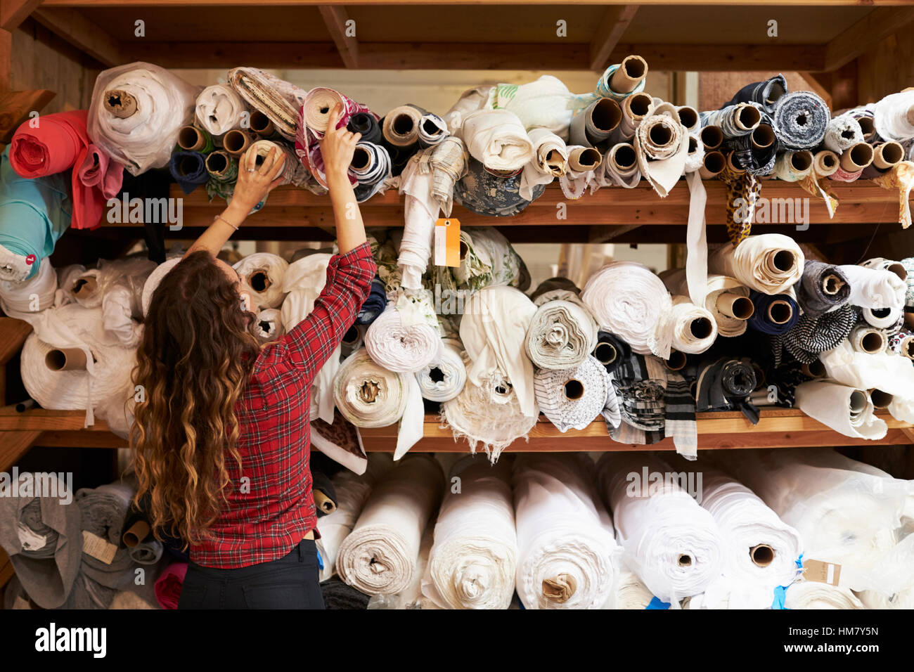 Young woman reaching to select fabric from storage shelves Stock Photo ...