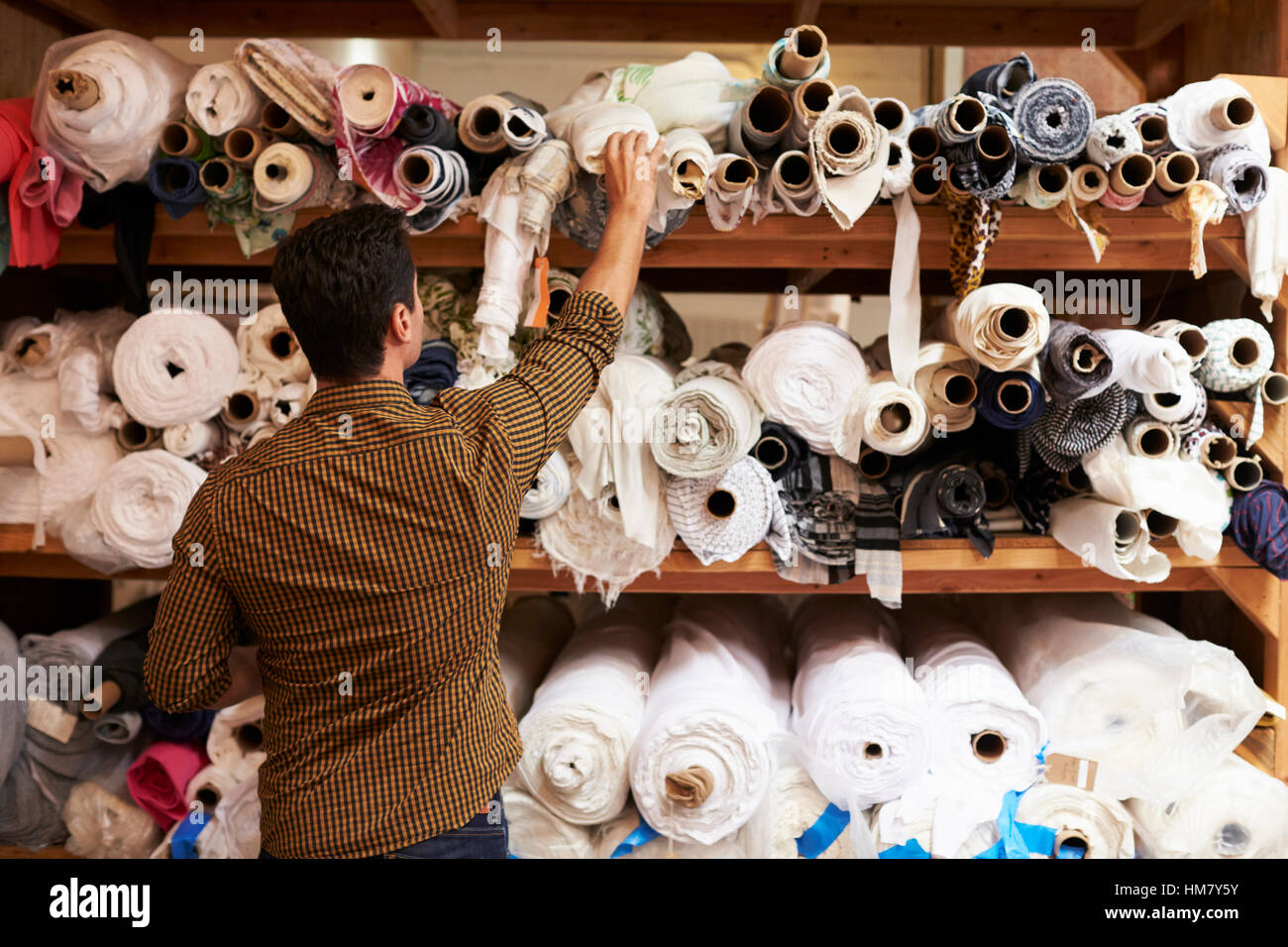 Man reaching to select fabric from storage shelves Stock Photo - Alamy