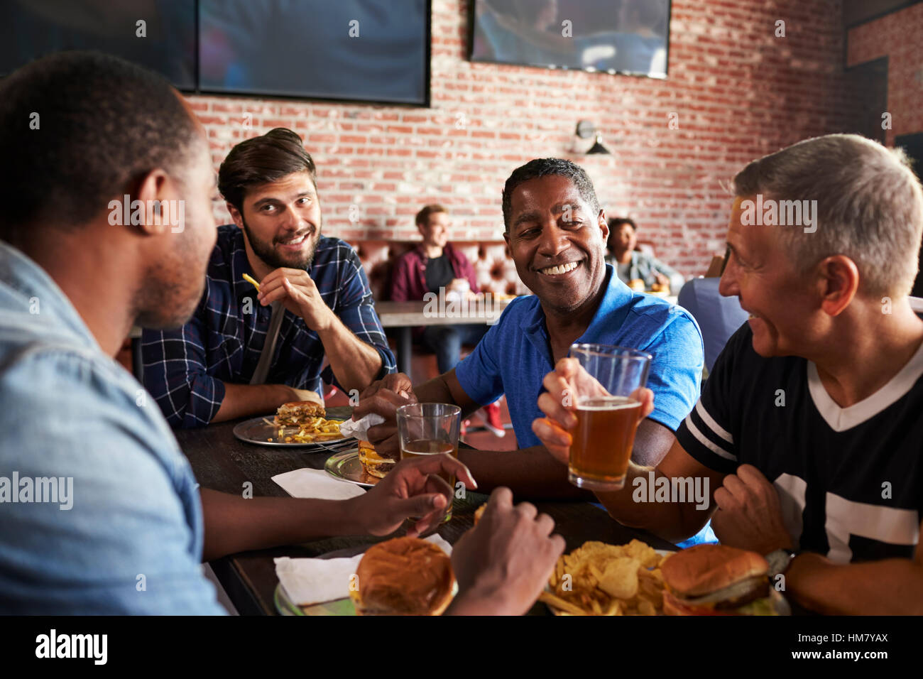 Male Friends Eating Out In Sports Bar With Screens In Behind Stock ...
