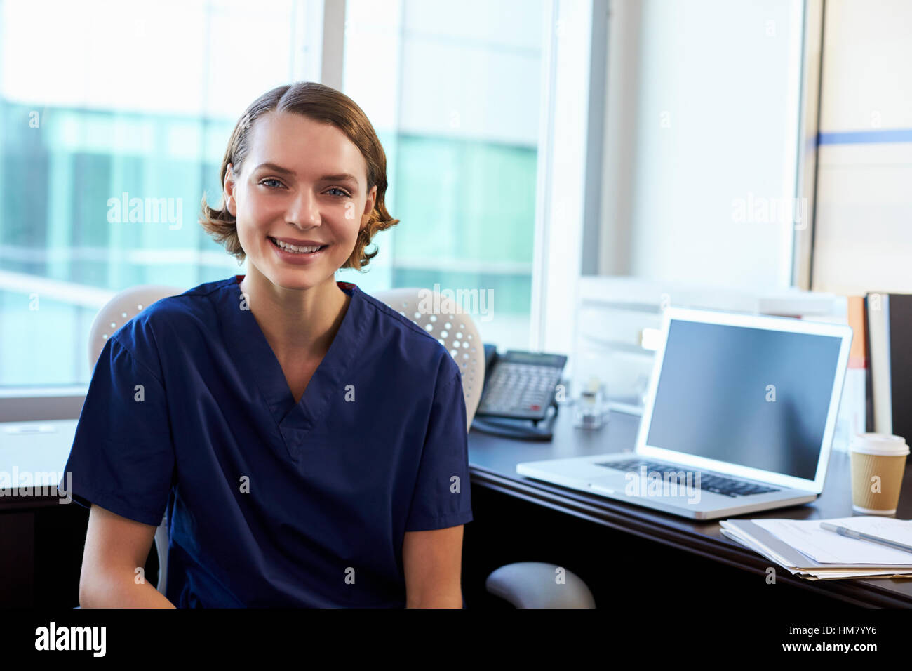 Portrait Of Nurse Wearing Scrubs Sitting At Desk In Office Stock Photo ...