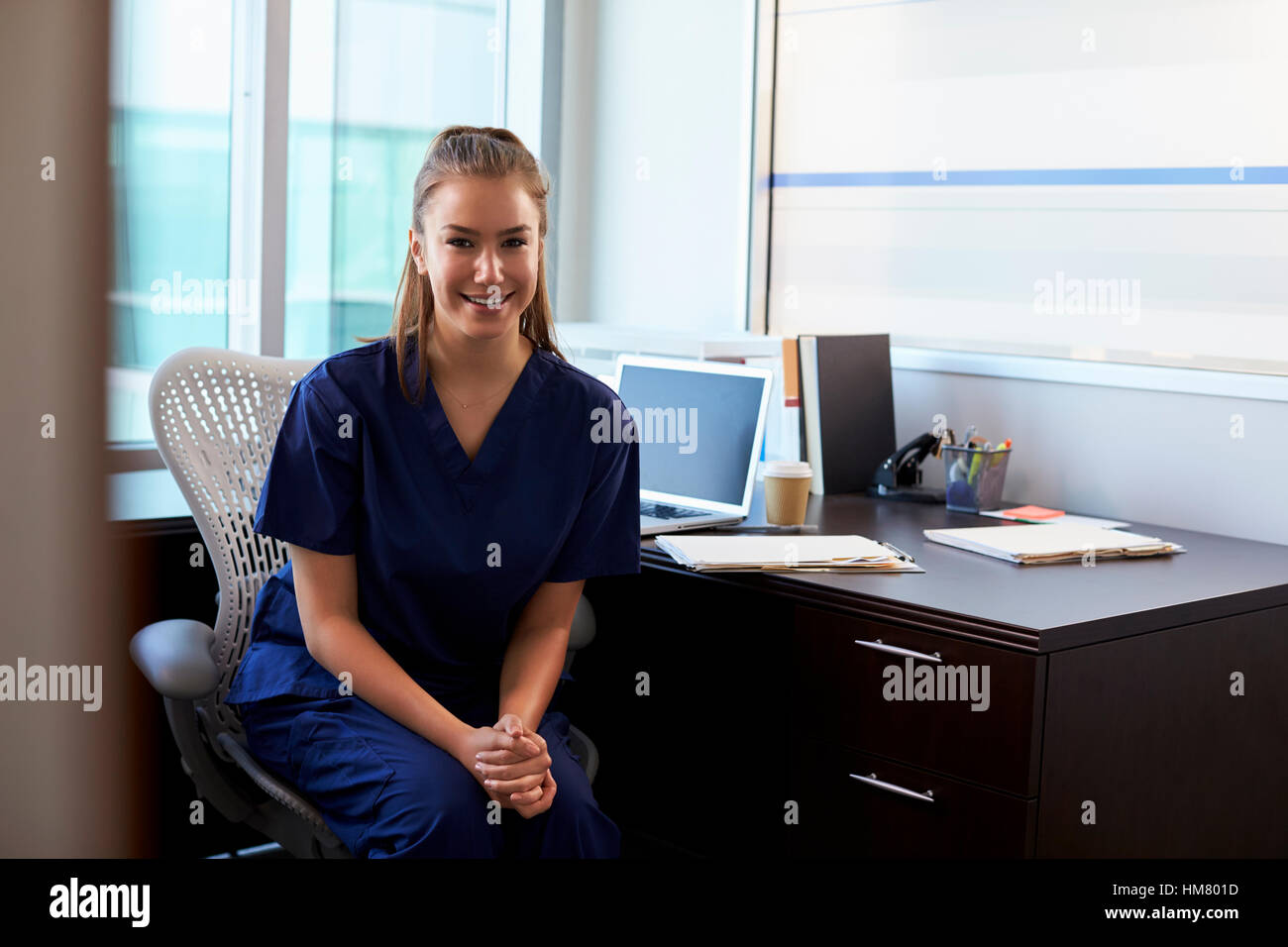 Portrait Of Nurse Wearing Scrubs Sitting At Desk In Office Stock Photo ...