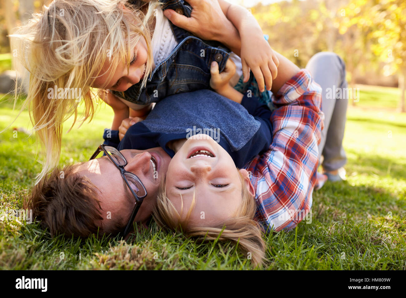 Two young kids lying on top of their dad in a park Stock Photo - Alamy