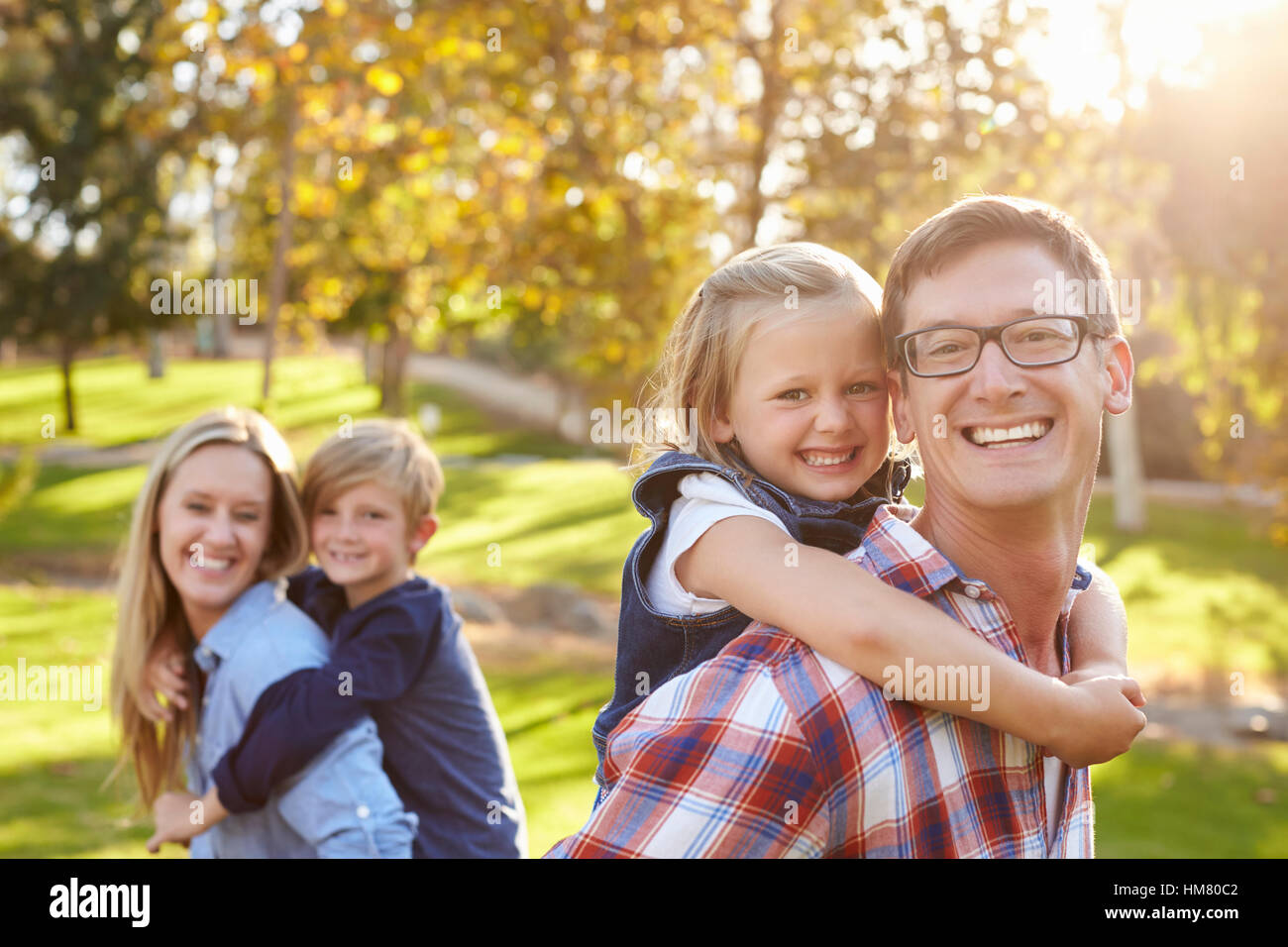 Parents carry their kids piggyback in a park selective focus Stock ...