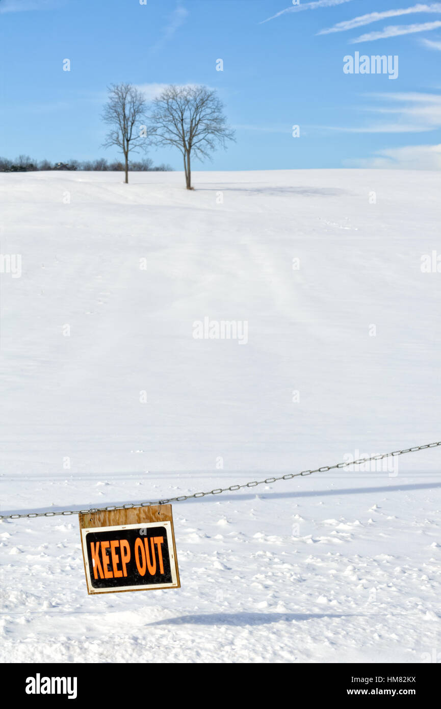 Keep Out sign chained across a snowy farm field in winter with two bare ...