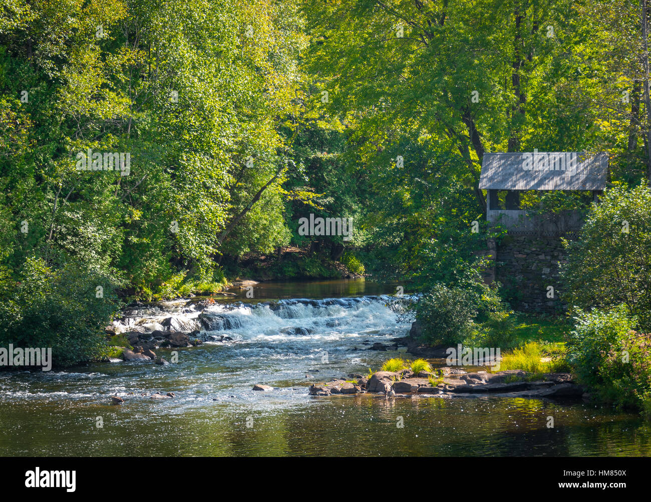 Old brick wall and watermill shed next to small woodland waterfall ...