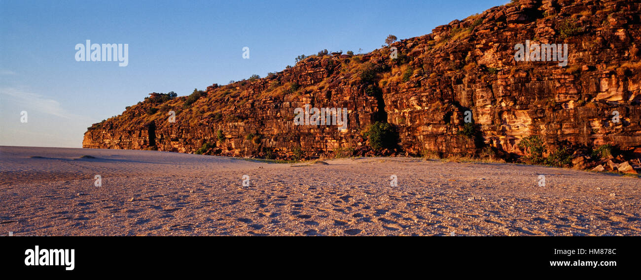 A rugged red sandstone cliff above a deserted beach at sunset Stock ...