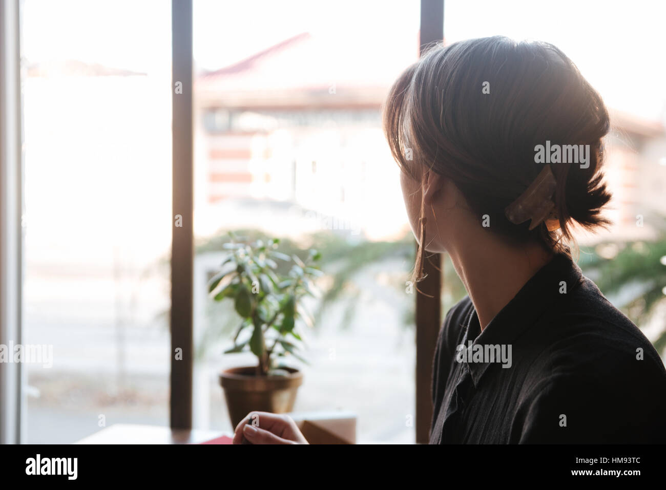 Back view image of young woman sitting at the table in cafe and looking ...