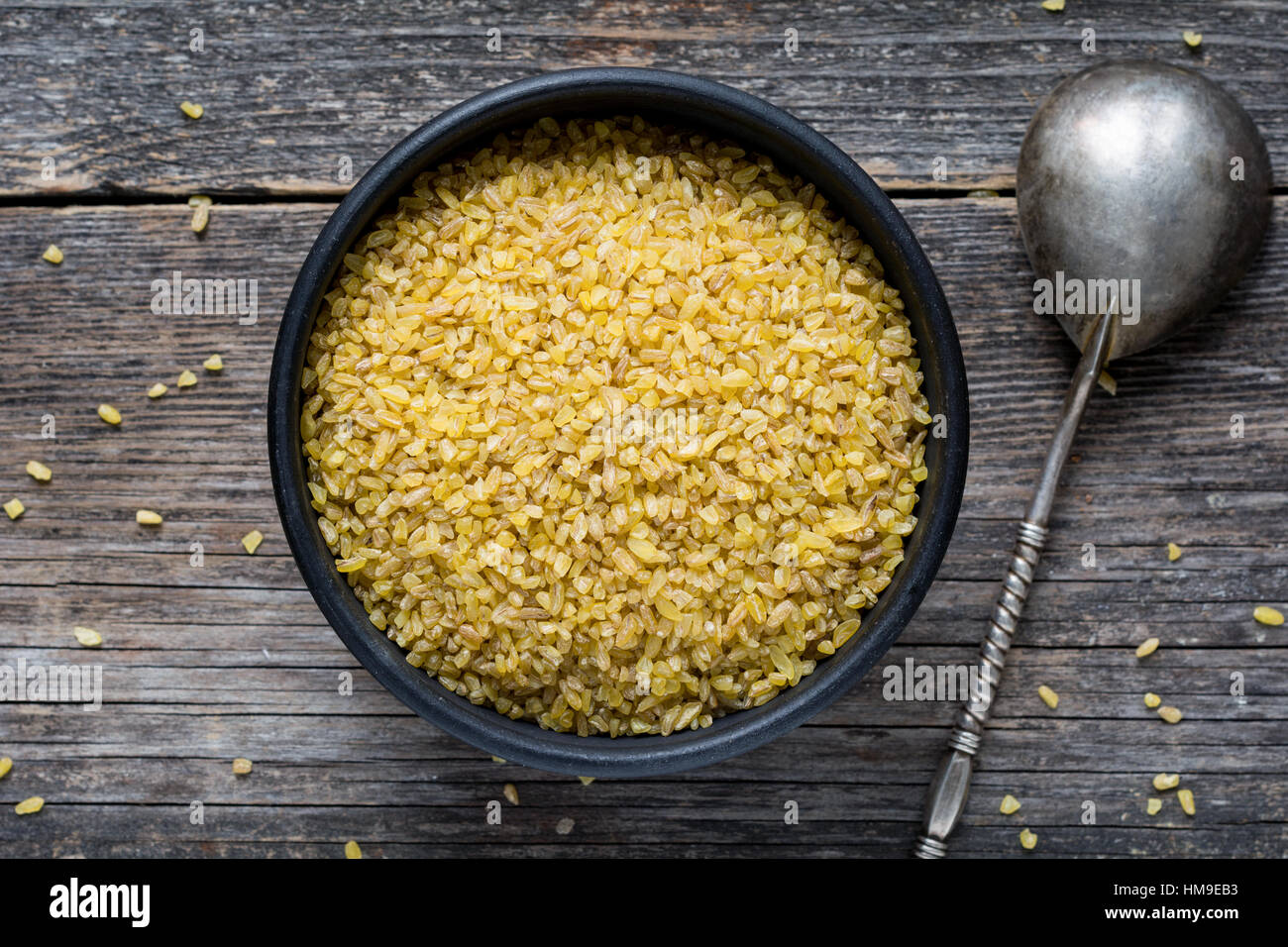 Bulgur, wheat grains in a bowl and vintage spoon on wooden background ...