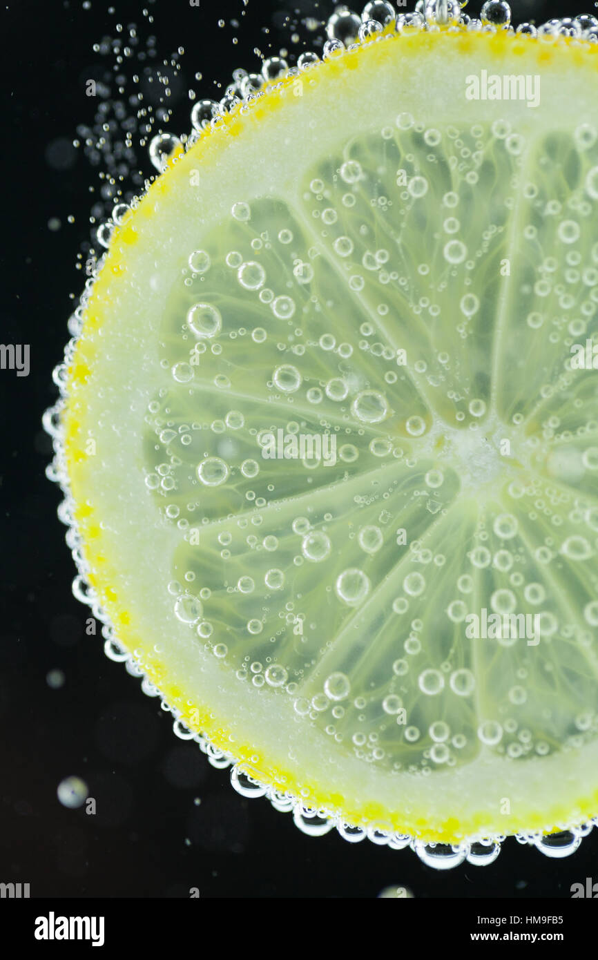 Close-up view of lemon slice under carbonated water with bubbles, refresher concept on black ...