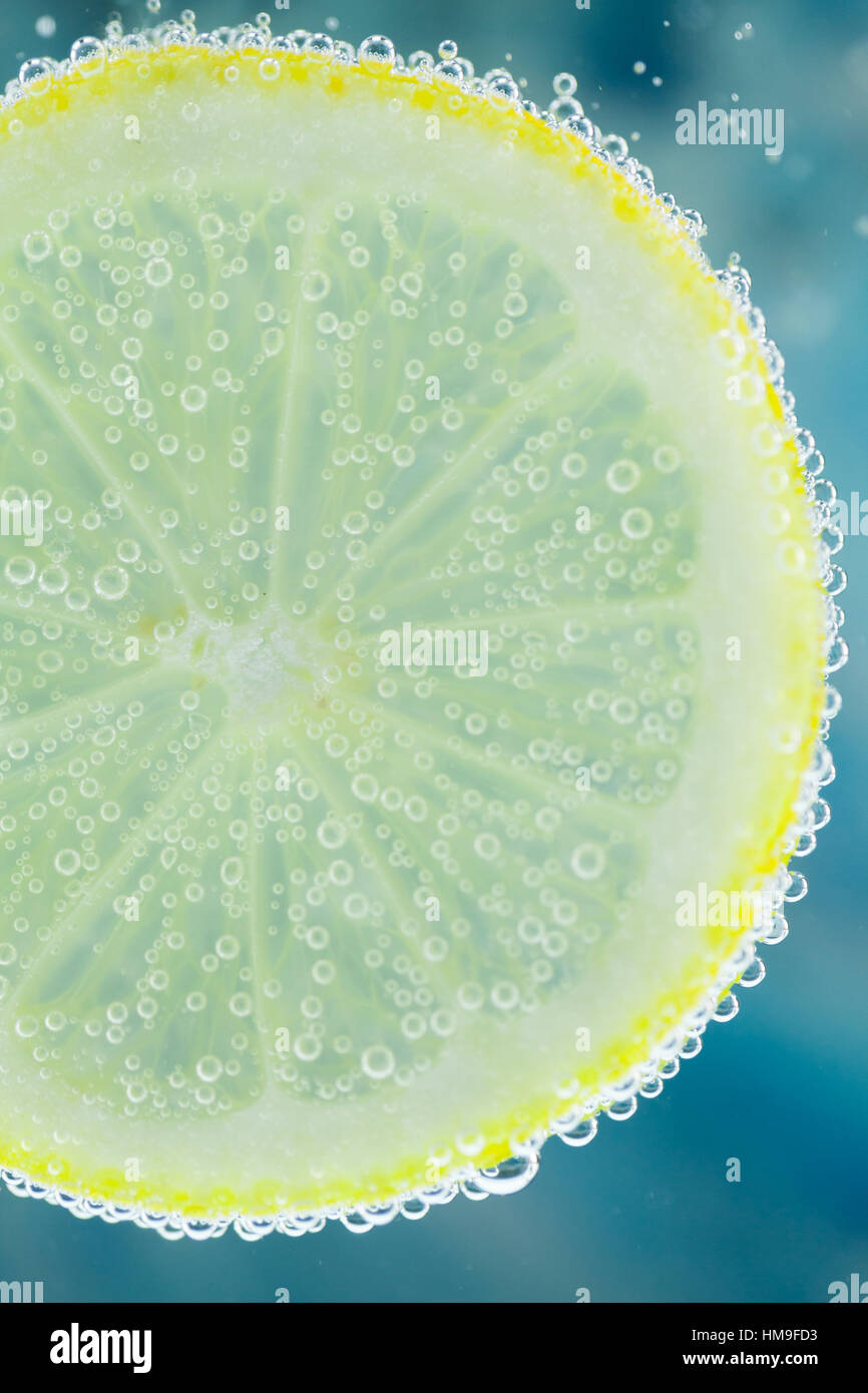 Vertical close-up of slice of lemon falling into carbonated water with ...