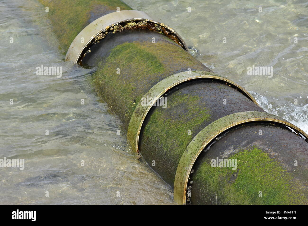 Large bore metal pipe entering sea at low angle on sandy shore with ...