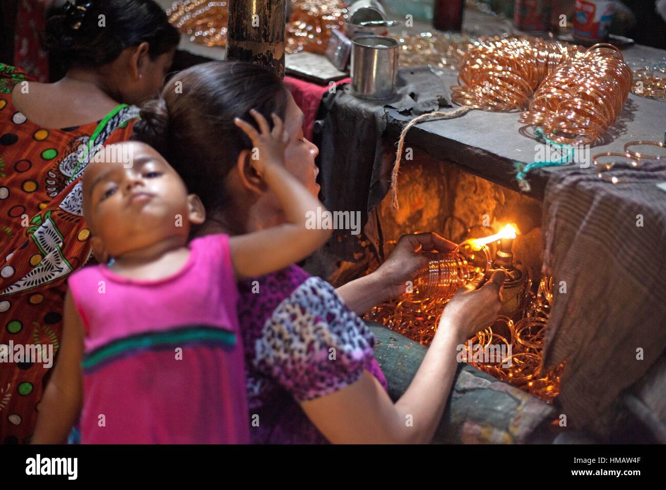 A working mother shapes glass in a small kiln at a glass bangle factory ...