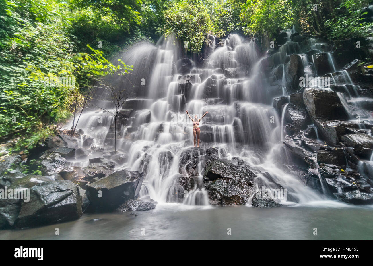 Woman standing on rock with outstretched arms, waterfall, Air Terjun ...