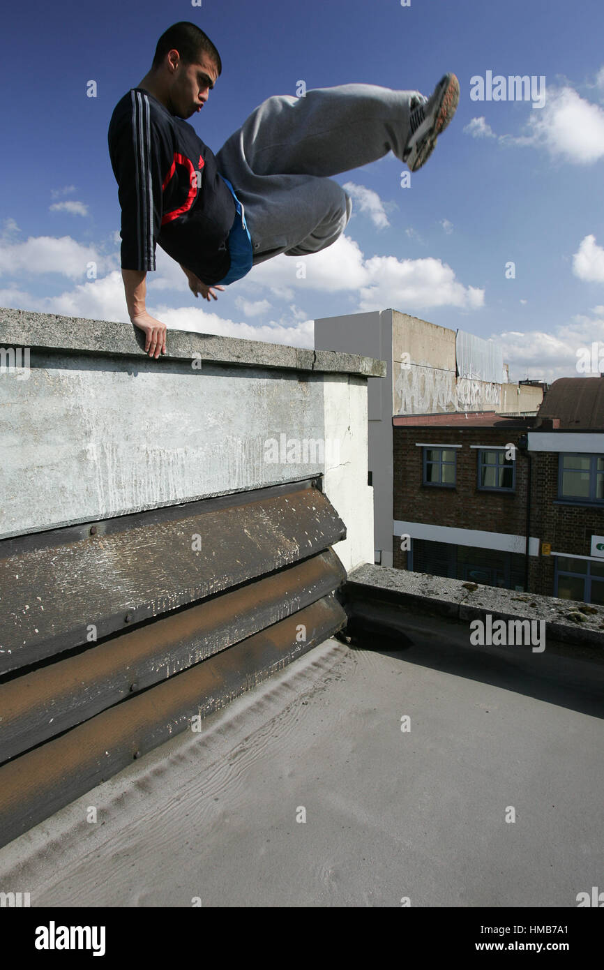 A parkour freerunning athlete vaulting over a wall on a rooftop with ...