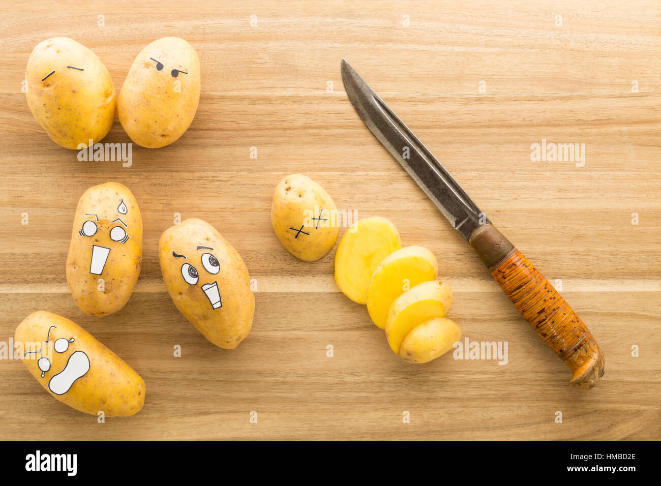 Fresh potatoes with cartoon style faces laying on a brown cutting board ...