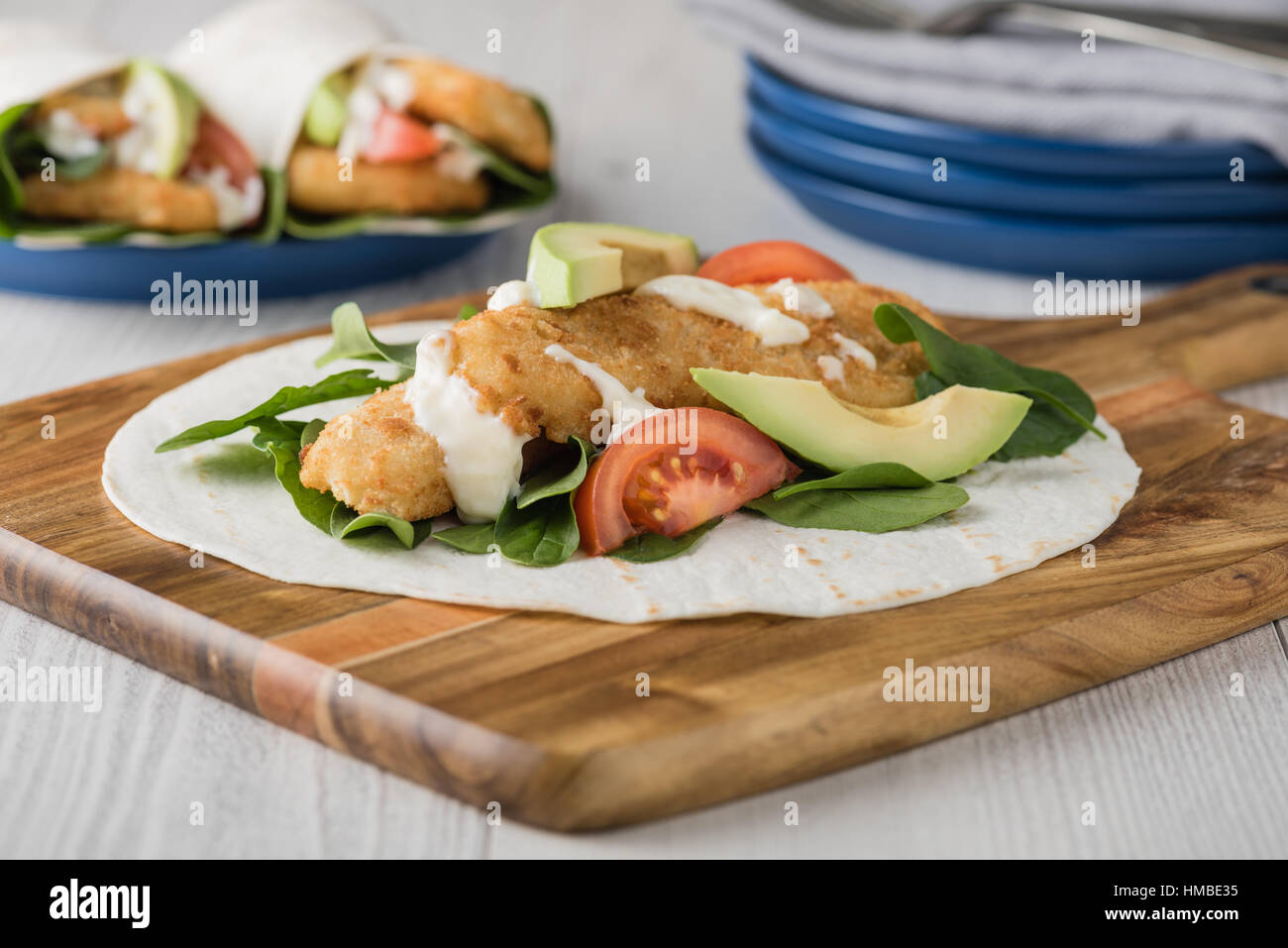 Fish finger wraps with avocado and tomato serves on wooden cheese ...