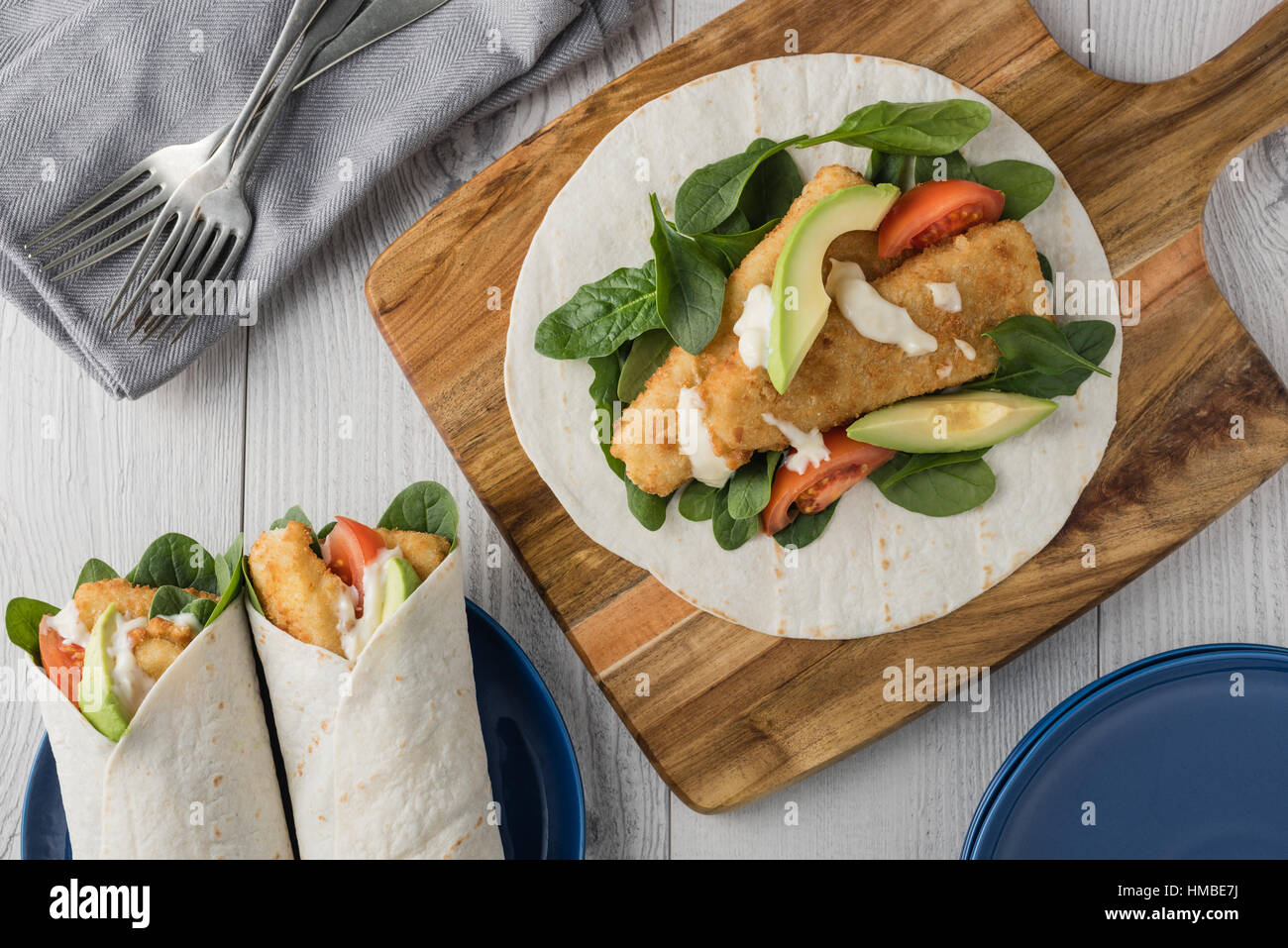 Fish finger wraps with avocado and tomato serves on wooden cheese ...