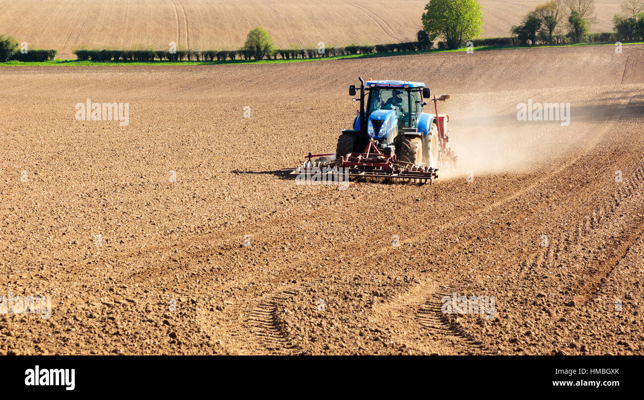 Tractor raking a ploughed field in spring ready for planting a crop ...