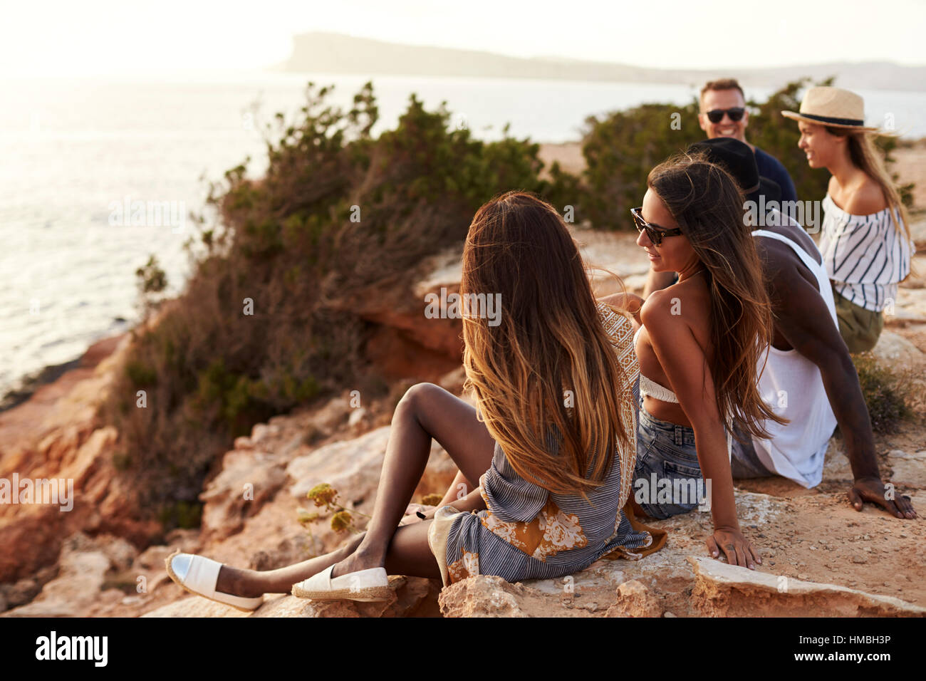 Rear View Of Friends Sitting On Cliff Watching Sunset Stock Photo - Alamy