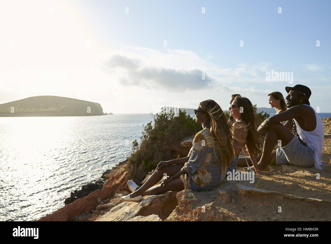 Side View Of Friends Sitting On Cliff Watching Sunset Stock Photo - Alamy