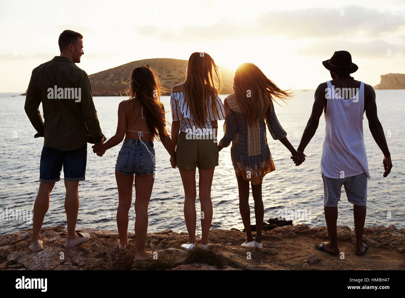 Rear View Of Friends Standing On Cliff Watching Sunset Stock Photo - Alamy