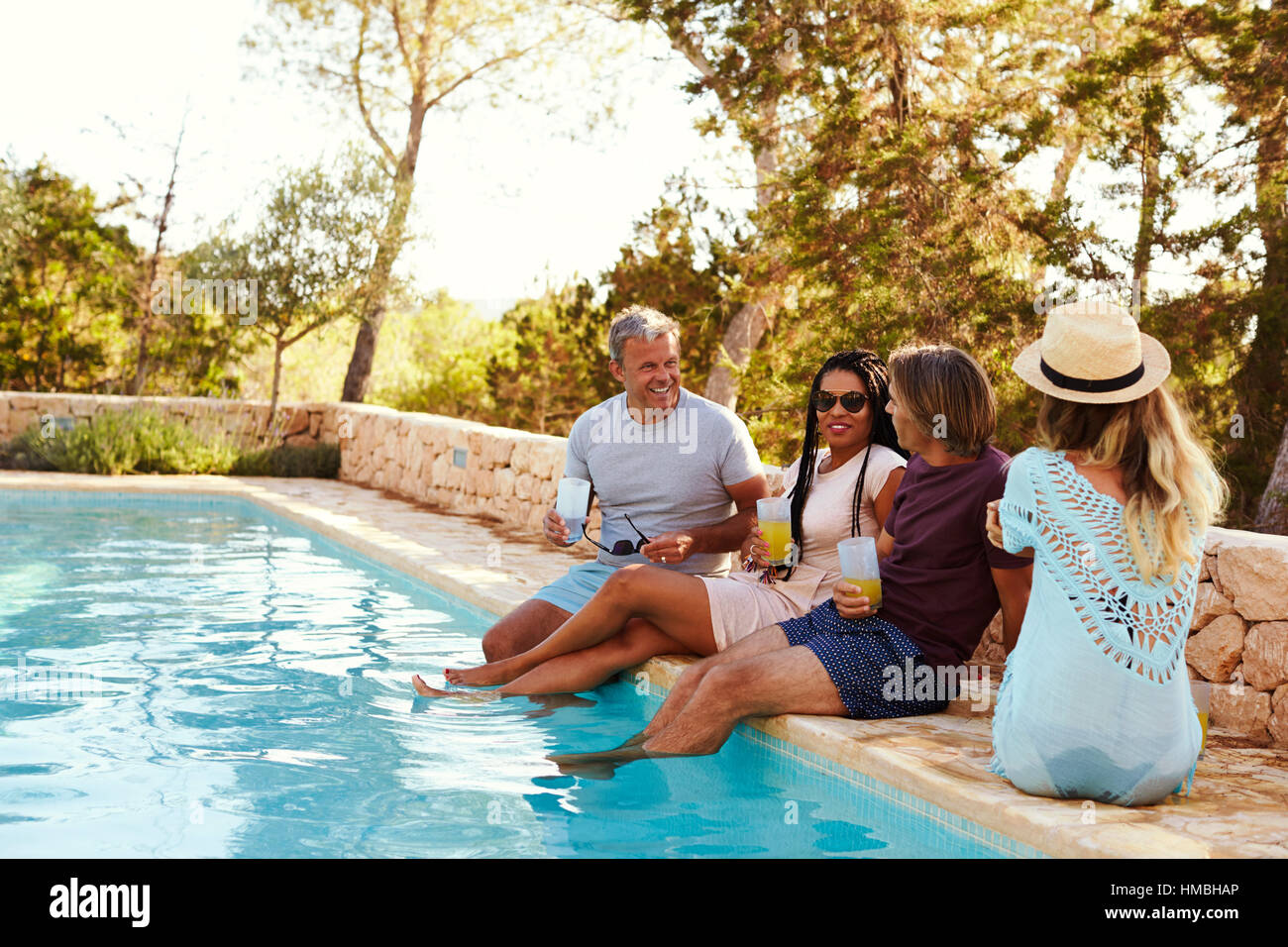 Two couples sitting at the edge of a swimming pool talking Stock Photo ...