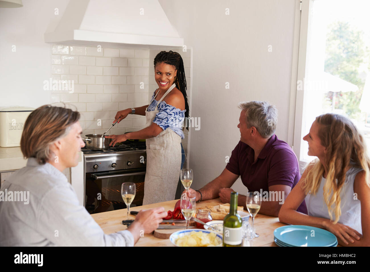 Friends drinking wine in kitchen while woman prepares food Stock Photo ...