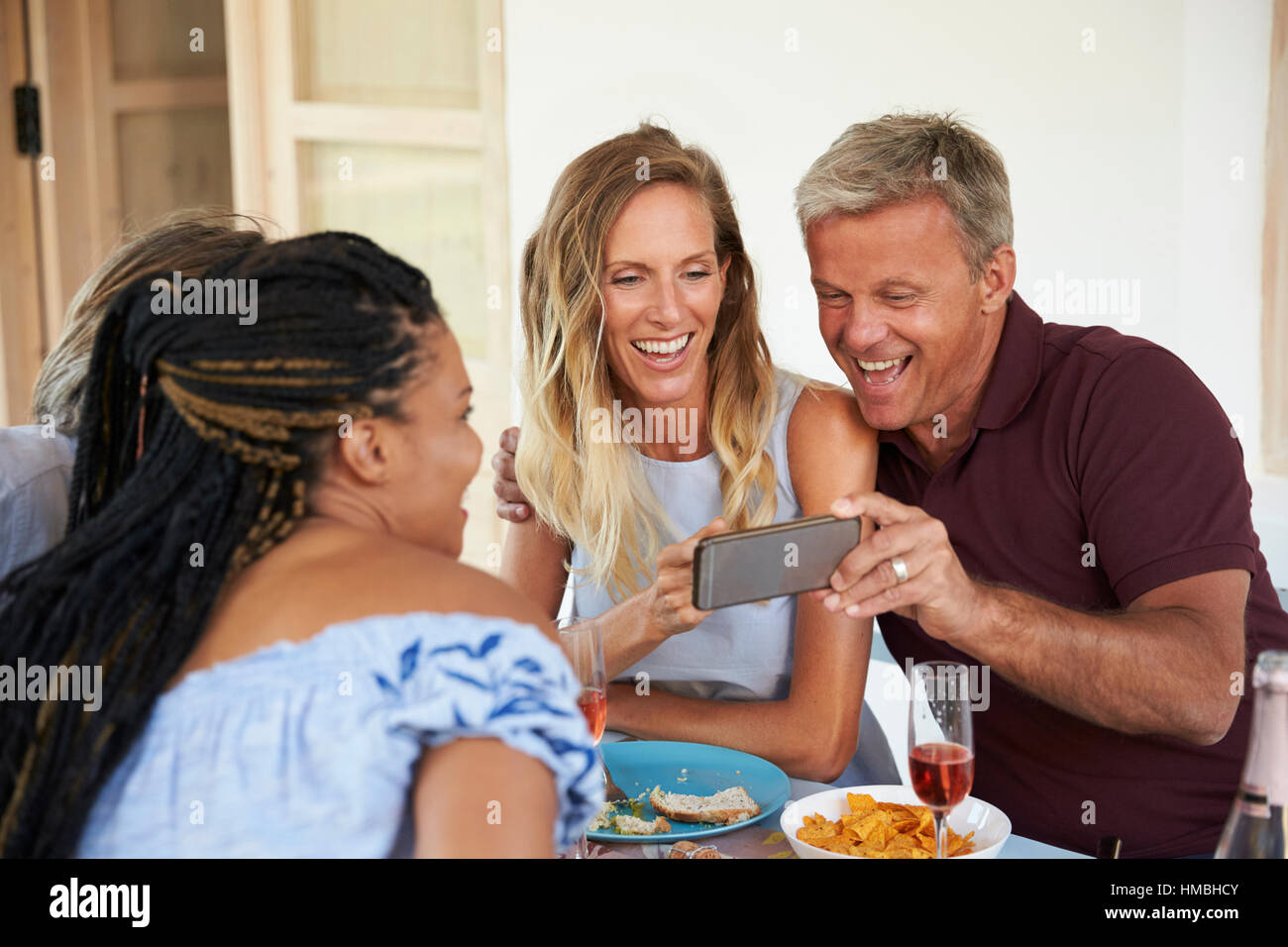 Friends at a dinner table look at pictures on a smartphone Stock Photo ...