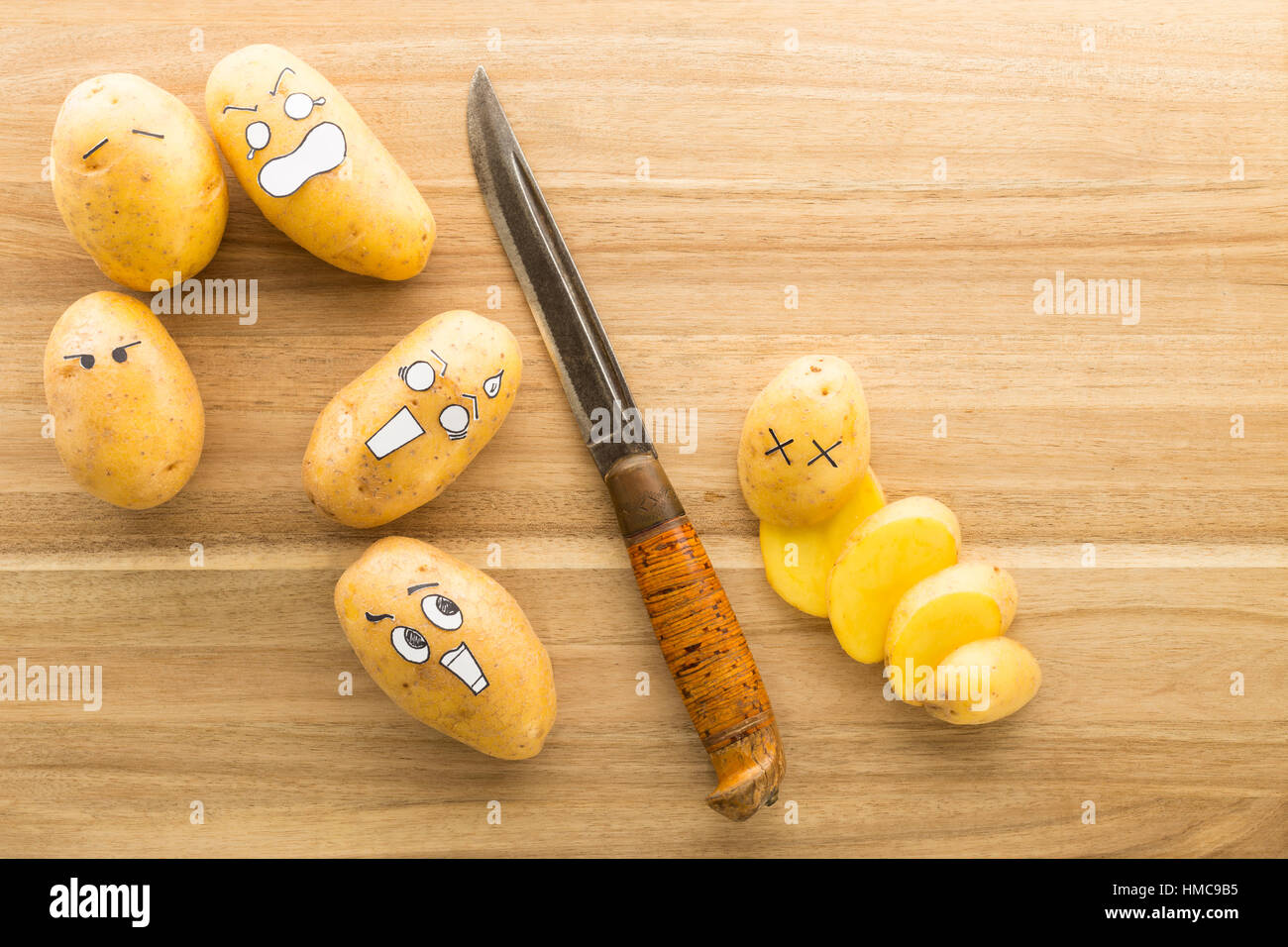 Fresh potatoes with cartoon style faces laying on a brown cutting board ...