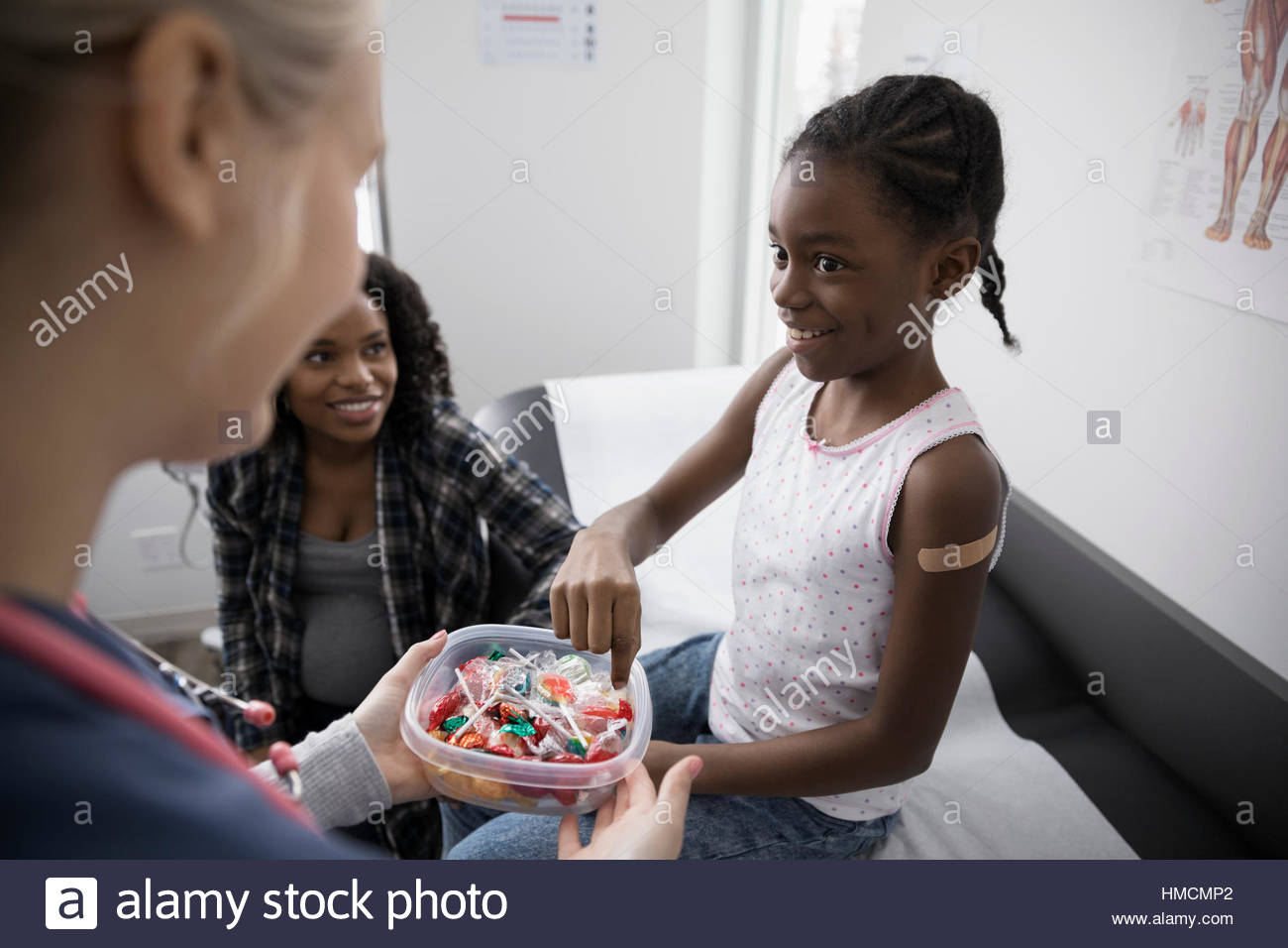 Female nurse offering girl patient candy in clinic examination room ...