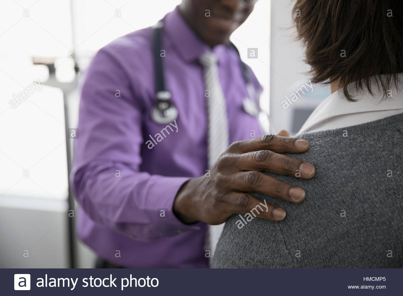 Caring male doctor touching shoulder of female patient in clinic ...
