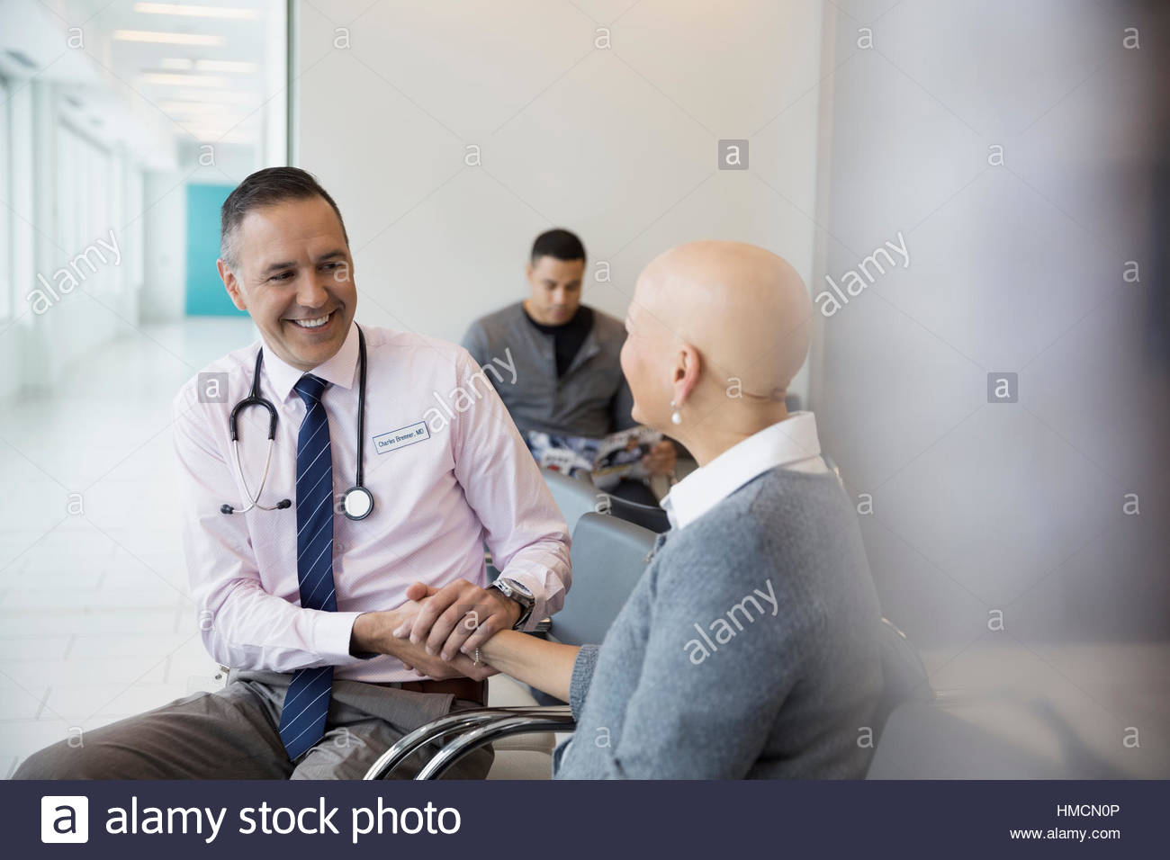 Smiling male doctor holding hands with bald female cancer patient in ...