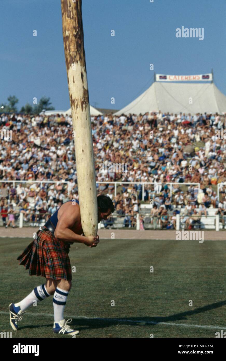 Athlete wearing a kilt carrying a caber (large tapered wooden pole ...