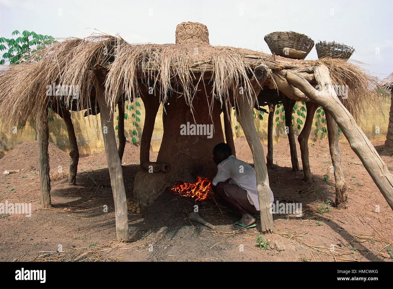 A Senufo blacksmith at work in a hut with a thatched roof, Ivory Coast ...