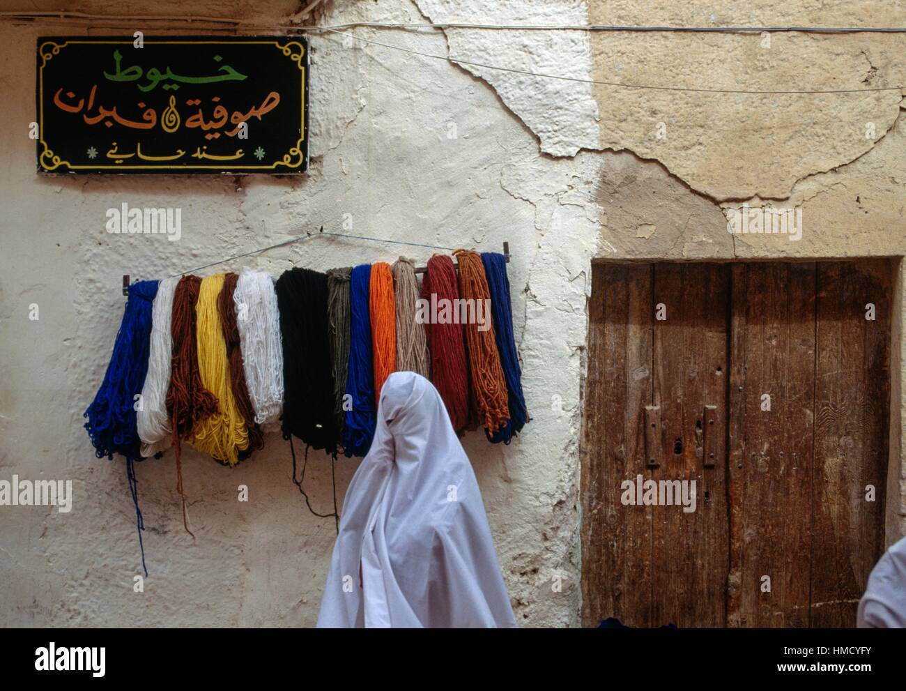 A woman wearing a burqa and skeins of wool hanging up, M'zab Valley ...
