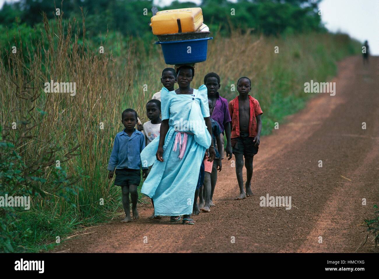 Woman with containers on her heads leading kids along a Kabalega road ...