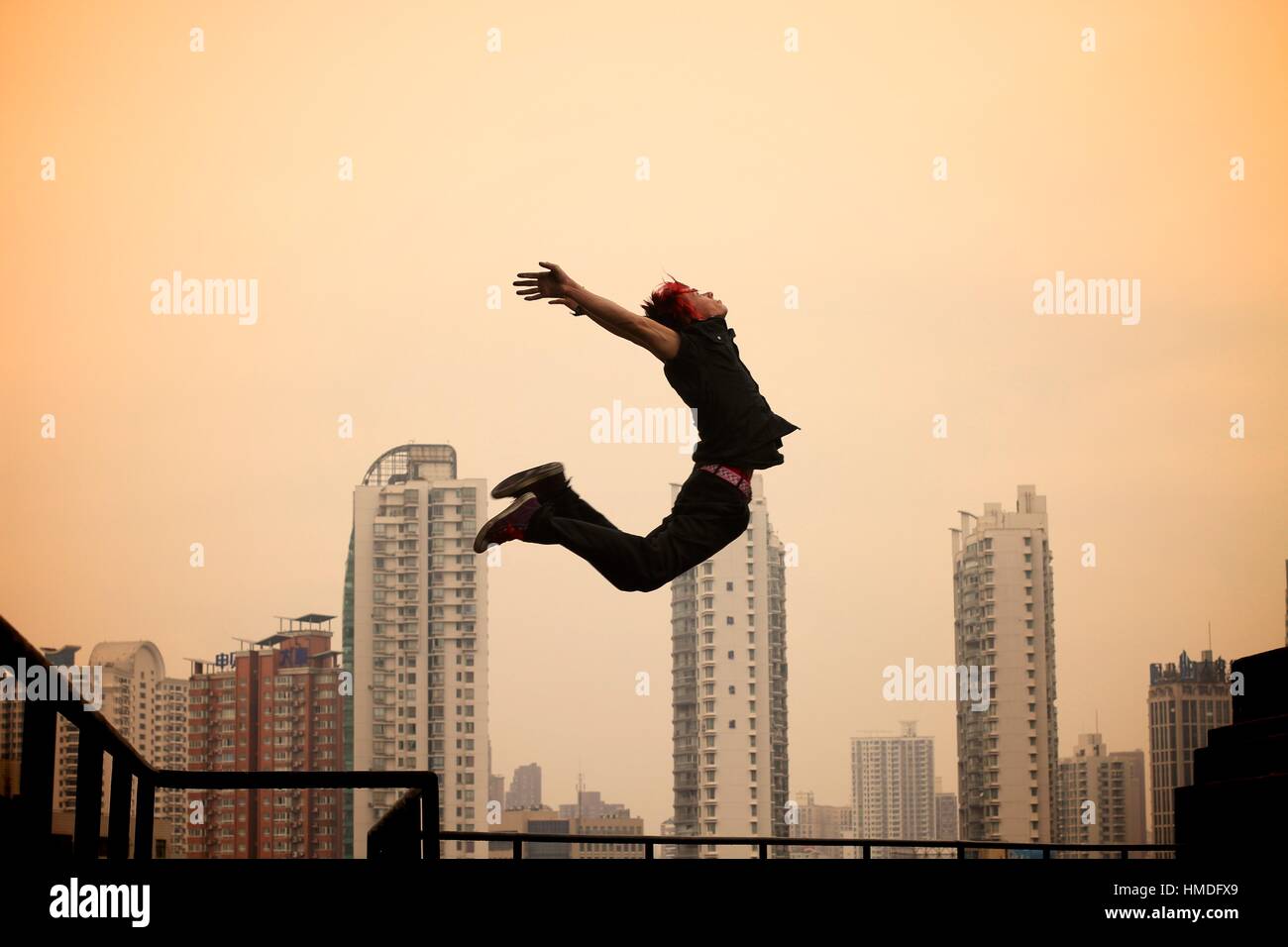 China, Shanghai, Young man performing parkour on roof of building Stock ...