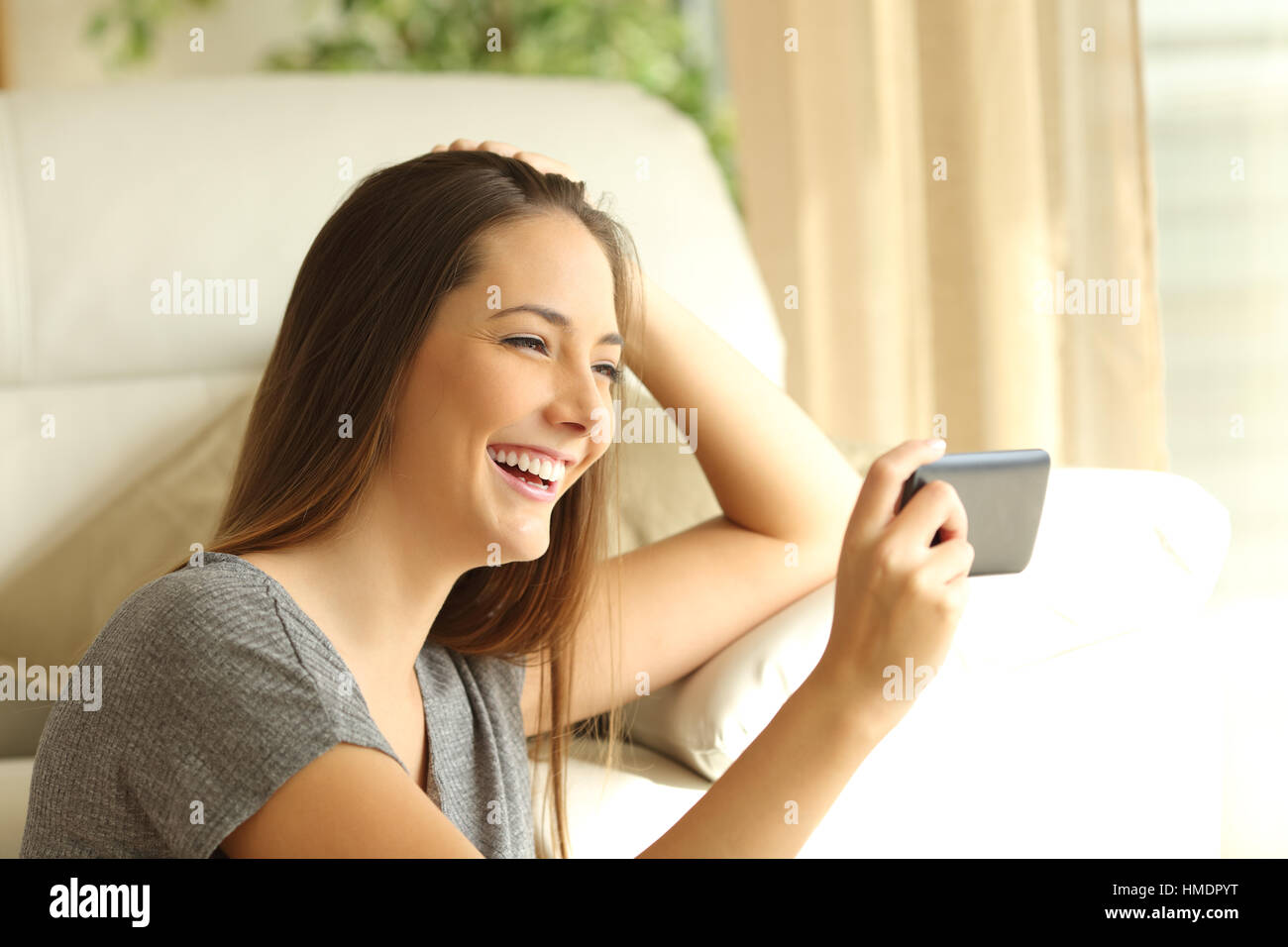 Girl watching streaming video in a smart phone sitting on the floor of ...