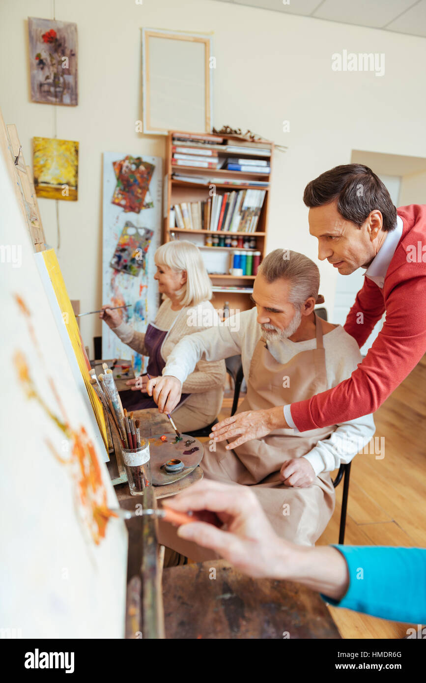 Joyful artist helping elderly man in painting studio Stock Photo - Alamy