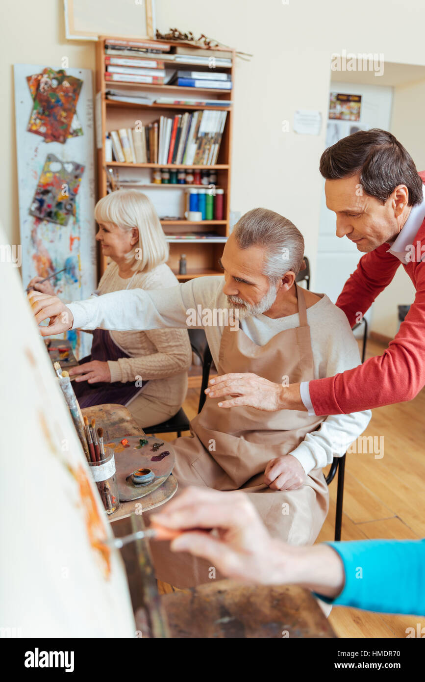 Talented artist helping elderly man in painting studio Stock Photo - Alamy