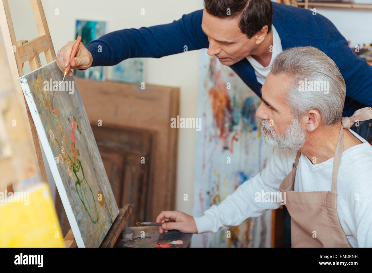 Concentrated artist helping elderly man in painting Stock Photo - Alamy