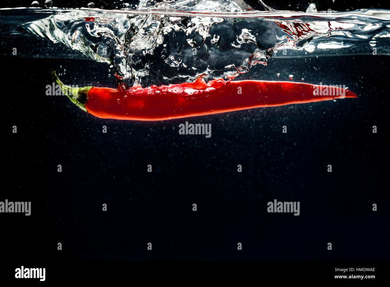 Red hot chili pepper splashing into water isolated on the black ...