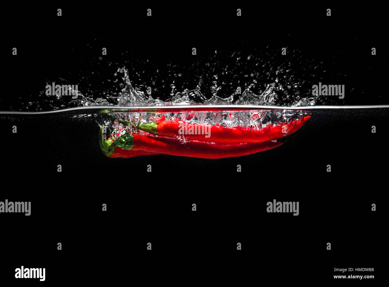Red hot chili peppers splashing into water isolated on the black ...