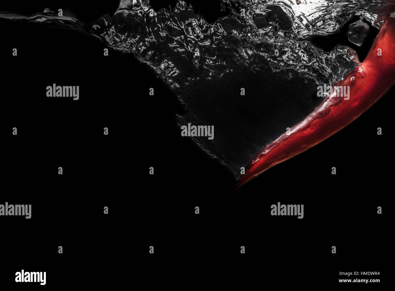 Red hot chili pepper splashing into water isolated on the black ...